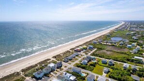 Vista aérea de uma área residencial costeira com casas, uma praia e céu claro.