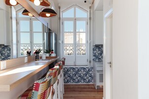 Uma cozinha moderna com bancada de madeira, um espelho grande e vista da cidade através de uma janela com grades de ferro decorativas.