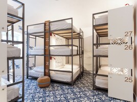 Um dormitório com beliches numerados de 19 a 27 e um piso estampado.
