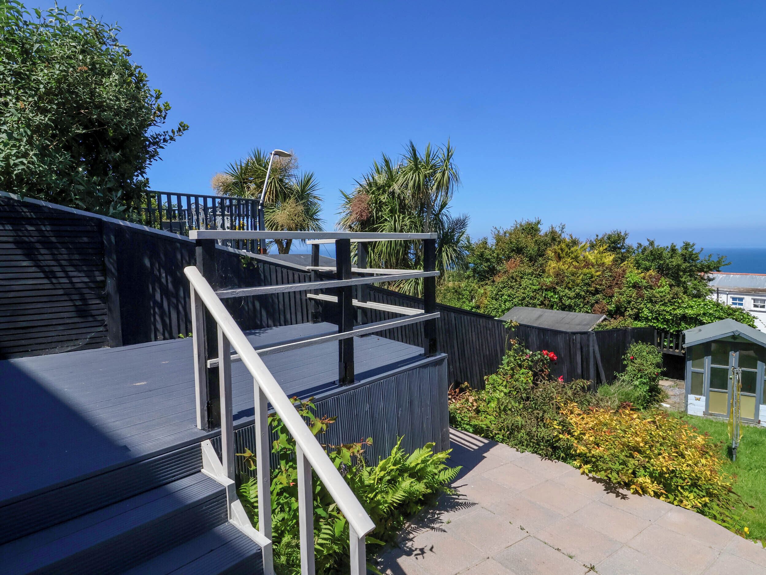 Escadaria que leva a um deck com vista para o mar, cercado por vegetação e um cercado de madeira.