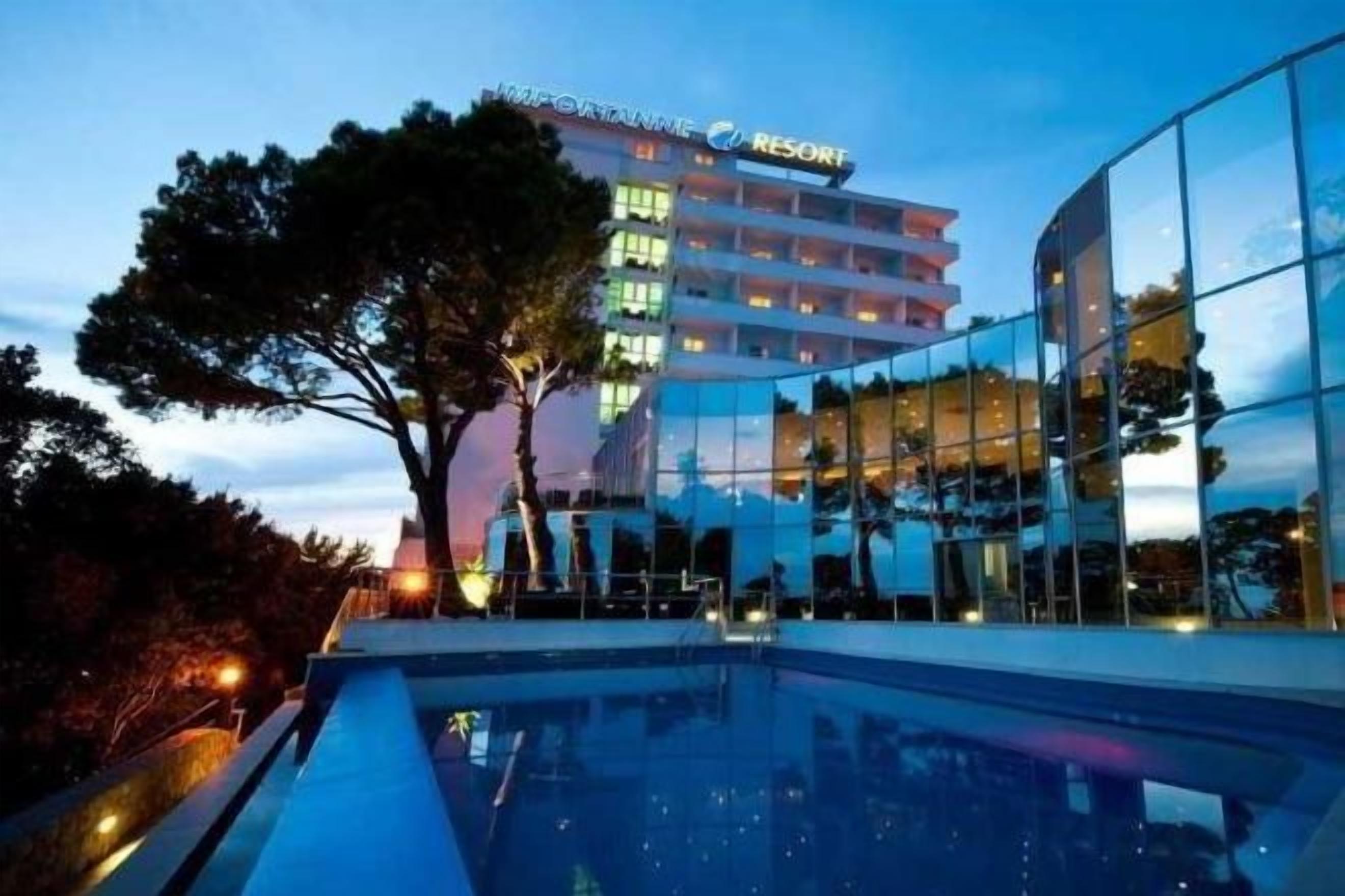 Um hotel moderno com piscina, grandes janelas de vidro e o reflexo do edifício.