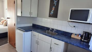 Uma cozinha compacta com armários brancos, bancada azul, micro-ondas, pia e uma pequena lixeira.