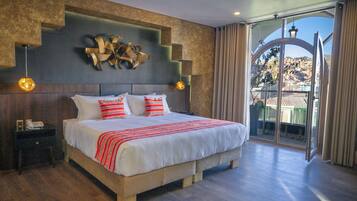 Um quarto espaçoso com uma cama grande, cabeceira de madeira e vista para uma encosta através de uma porta de vidro deslizante.