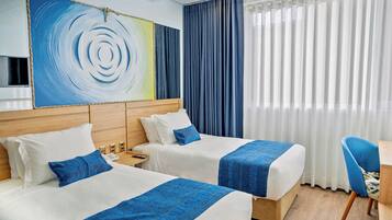 Quarto de hotel com duas camas, uma pintura abstrata grande, cabeceira de madeira, escrivaninha e uma cadeira.