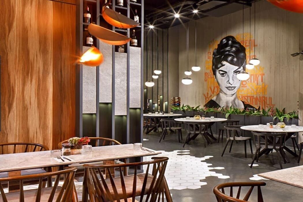 Interior de restaurante com paredes de madeira, luminárias pendentes e um mural na parede do fundo.