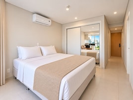 Quarto de hotel com uma cama grande, ar condicionado e vista da cidade através de uma porta de vidro.