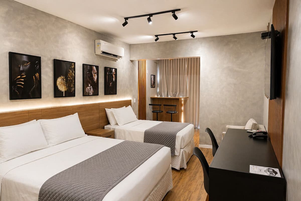 Quarto de hotel com duas camas, uma escrivaninha, televisão e obras de arte na parede.