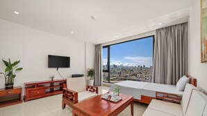 Quarto de hotel moderno com uma grande janela, televisão de tela plana, sofá-cama, mesa de centro de madeira e um pequeno rack para televisão.