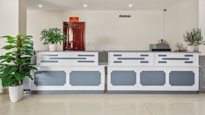 Uma área de recepção com porta de madeira, balcão branco com painéis cinzas e plantas em vasos.