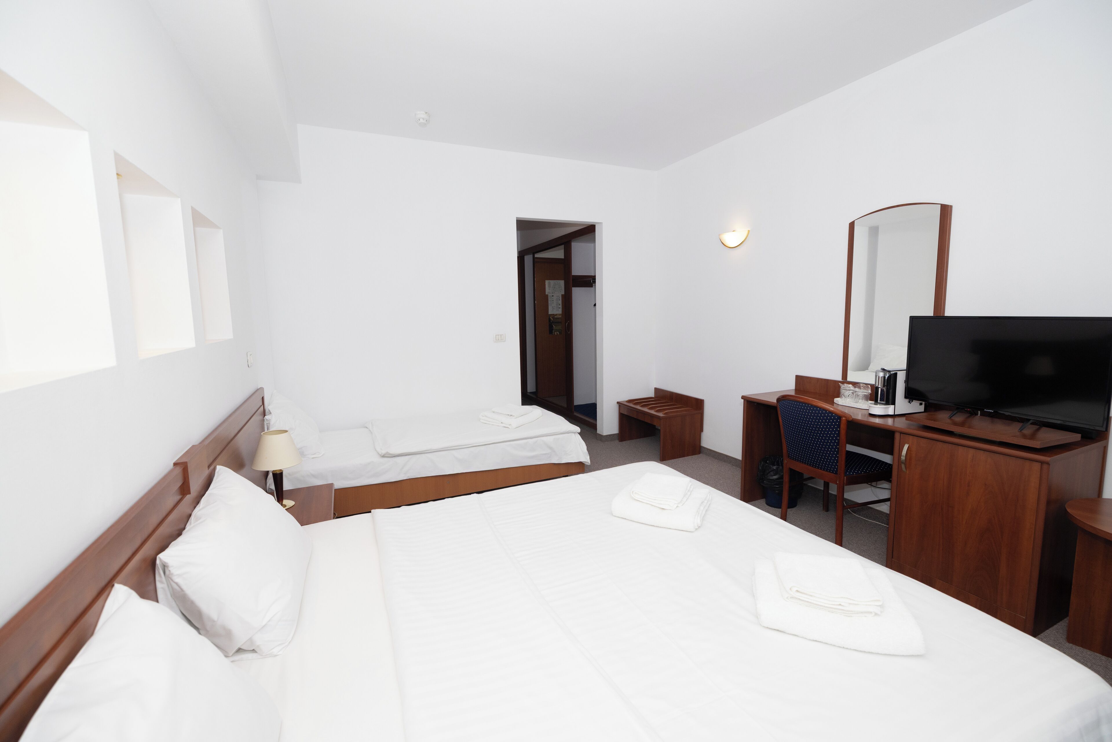 Quarto de hotel com uma cama grande, uma mesa de escritório com um computador, uma televisão e um pequeno espaço de estar.