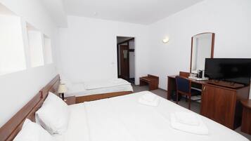 Quarto de hotel com uma cama grande, uma mesa de escritório com um computador, uma televisão e um pequeno espaço de estar.