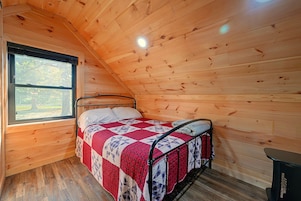 Uma cama de solteiro com estrutura de metal em um quarto com paredes de madeira e teto inclinado.