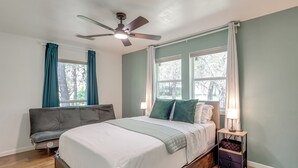 Quarto com cama, ventilador de teto, mesa de cabeceira com luminária e janela com cortinas.