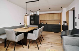 Uma cozinha moderna com armários de madeira, uma ilha central e uma área de jantar com cadeiras estofadas cinzas e mesa de madeira.