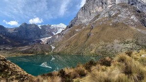 Paisagem montanhosa com um lago límpido, terreno acidentado e picos nevados.
