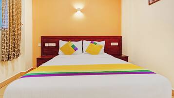 Cama bem arrumada com colcha listrada em branco e amarelo, dois travesseiros com padrões geométricos e cabeceira de madeira.