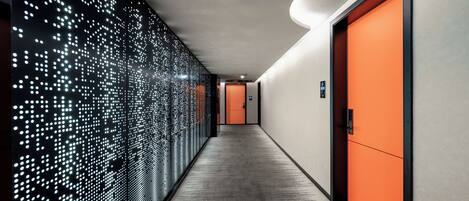 Um corredor com uma parede de LED estampada, piso de concreto e portas laranja.