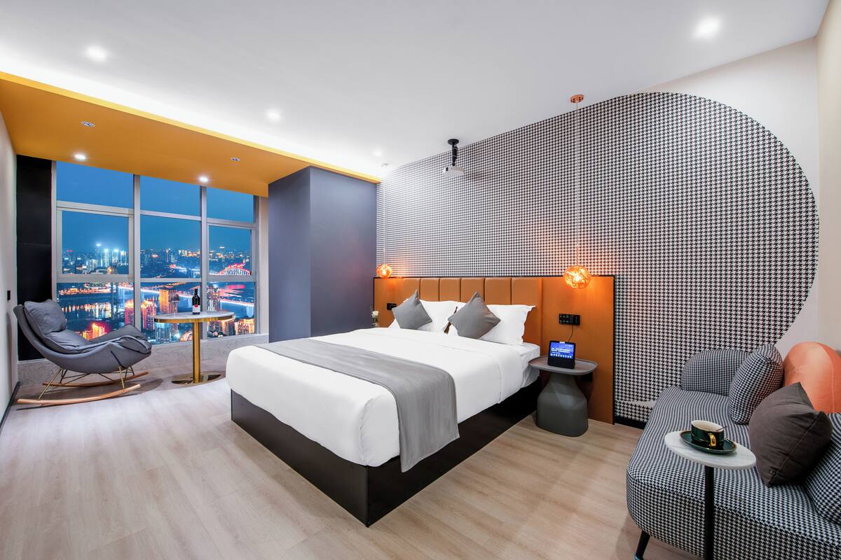 Quarto de hotel moderno com uma cama grande, vista para a cidade, uma mesa redonda e um espaço de estar acolhedor.