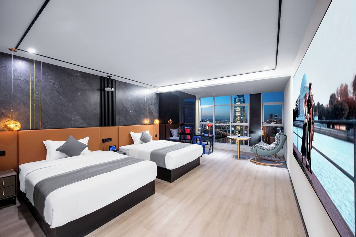 Quarto de hotel moderno com duas camas, uma escrivaninha e vista para a paisagem urbana.