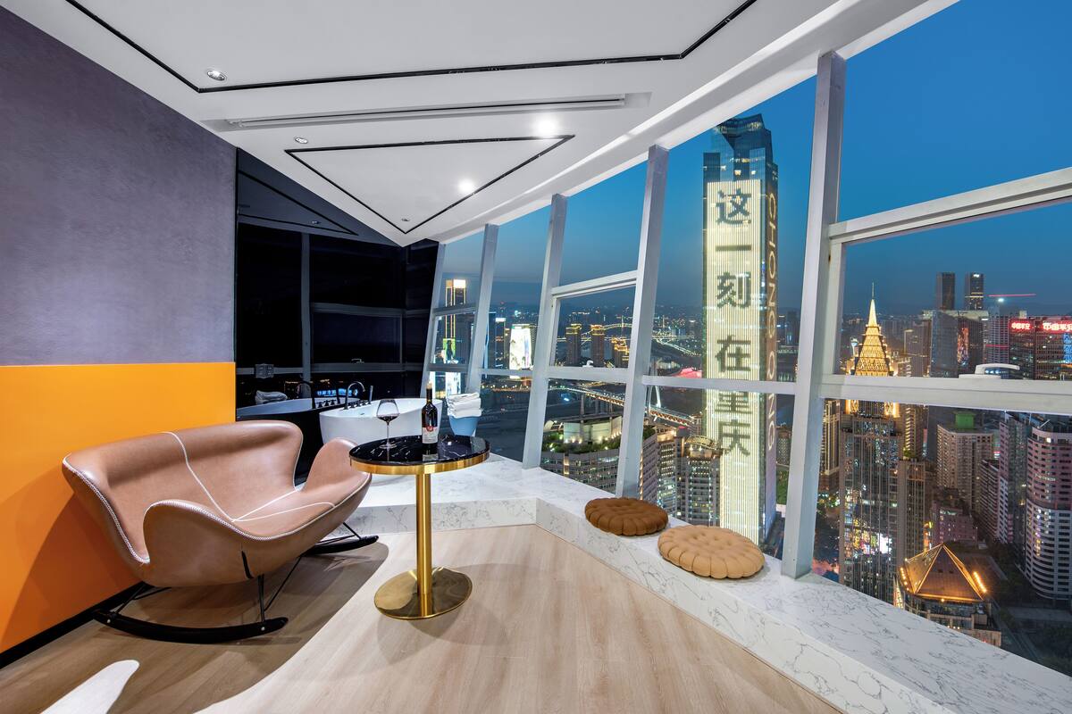 Quarto moderno com vista para a cidade, uma poltrona de couro, uma mesa redonda pequena e um painel de parede em mármore.