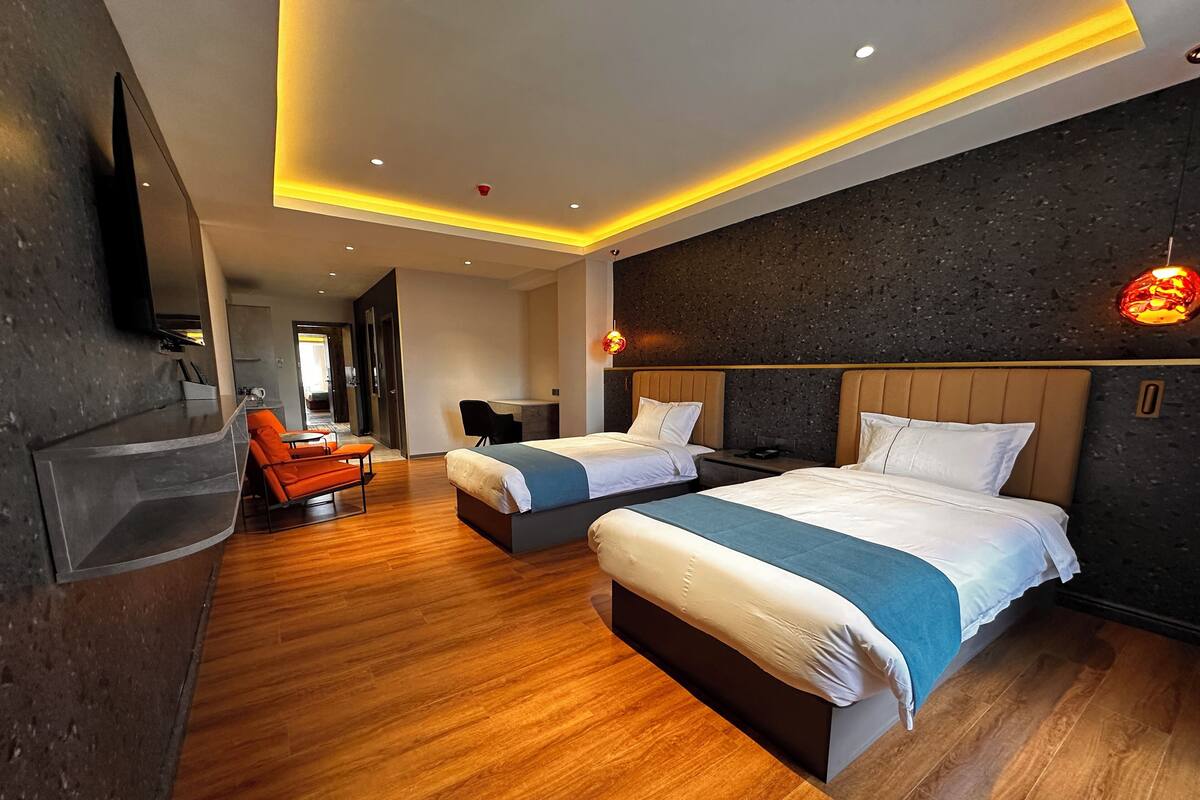 Quarto de hotel moderno com duas camas, uma mesa e uma área de estar.