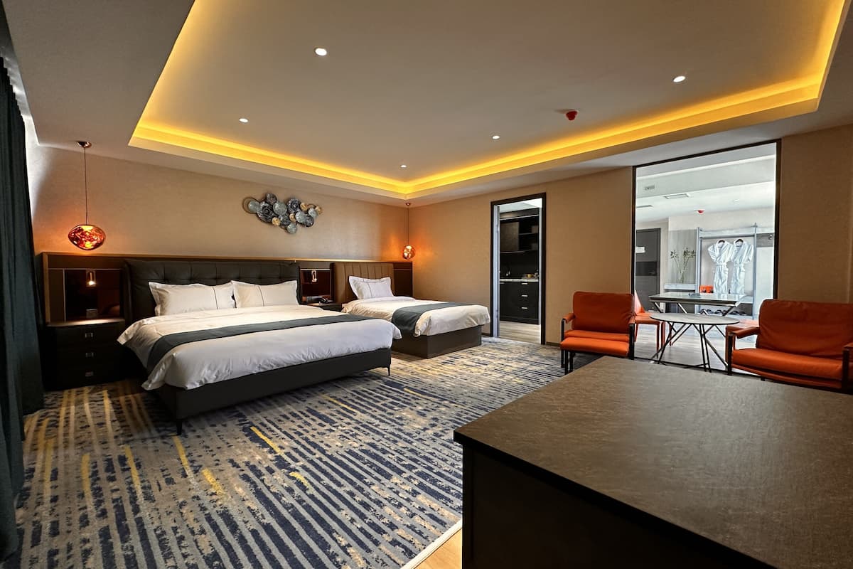 Quarto de hotel moderno com duas camas, uma área de estar e vista para um banheiro.