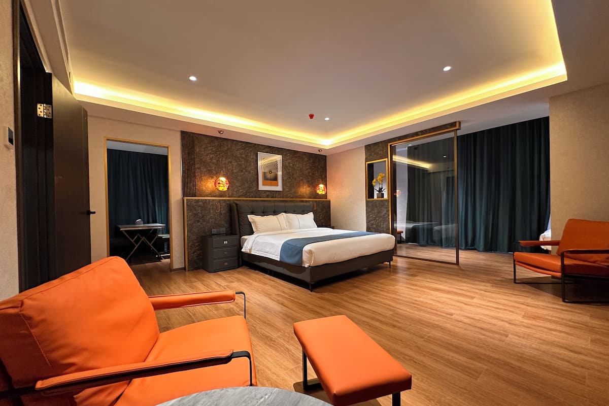 Quarto de hotel moderno com uma cama grande, uma escrivaninha, um sofá laranja e um banco.