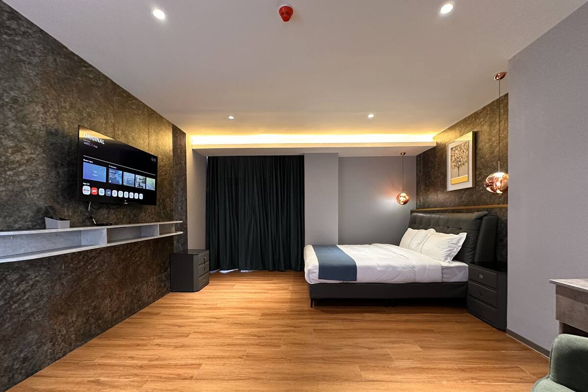 Quarto de hotel moderno com uma cama grande, televisão de tela plana na parede, escrivaninha com cadeira e cortina escura.