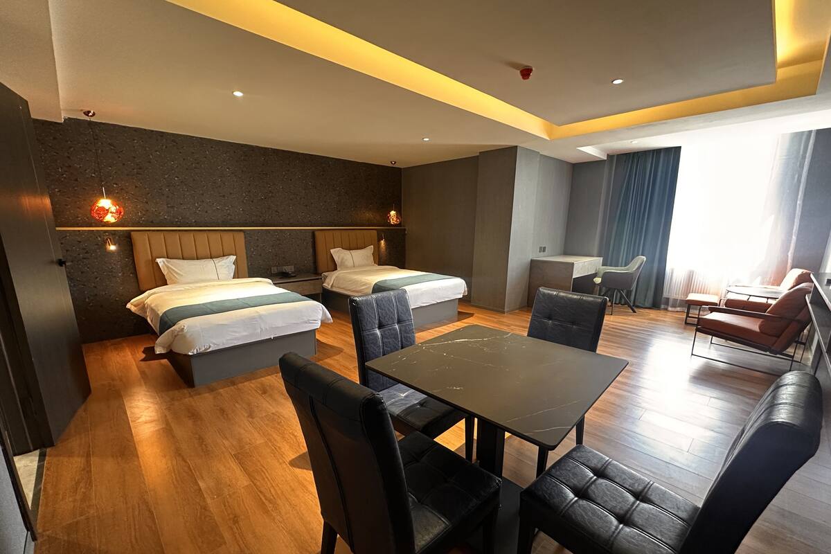 Quarto de hotel moderno com duas camas, uma mesa de jantar e um espaço de estar.