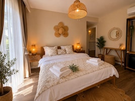 Quarto com cama grande, luminárias de cabeceira, luminária na parede, uma mesinha com uma planta e um espelho.