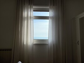 Quarto com janela coberta por cortinas leves, radiador e porta.