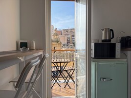 Varanda com vista para edifícios, pequena cozinha equipada com micro-ondas, chaleira e torradeira, e uma cadeira.