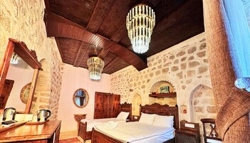 Quarto tradicional com cama, móveis de madeira, paredes de pedra e um candelabro.