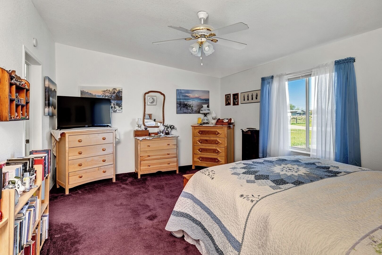 Um quarto com uma cama, duas cômodas de madeira, uma televisão e uma janela com cortinas.