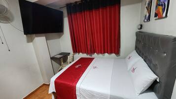 Quarto com cama, televisão, mesinha e uma cadeira.