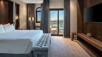 Quarto de hotel com uma cama grande, um banco, uma TV, uma mesa de trabalho e varanda com vista.