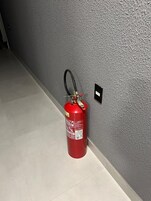 Um extintor de incêndio vermelho fixado numa parede cinza texturizada em um corredor.