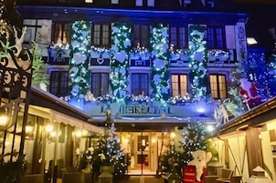 Fachada de hotel com decorações natalinas iluminadas, entrada central e placa acima da entrada.