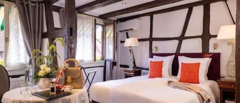 Quarto de hotel com uma cama grande, uma escrivaninha com cadeira, uma mesa com um vaso de flores e uma janela com cortinas.