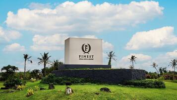 Placa para 'FINEST GUAM GOLF & RESORT', com base de pedra, cercada por vegetação exuberante e palmeiras.
