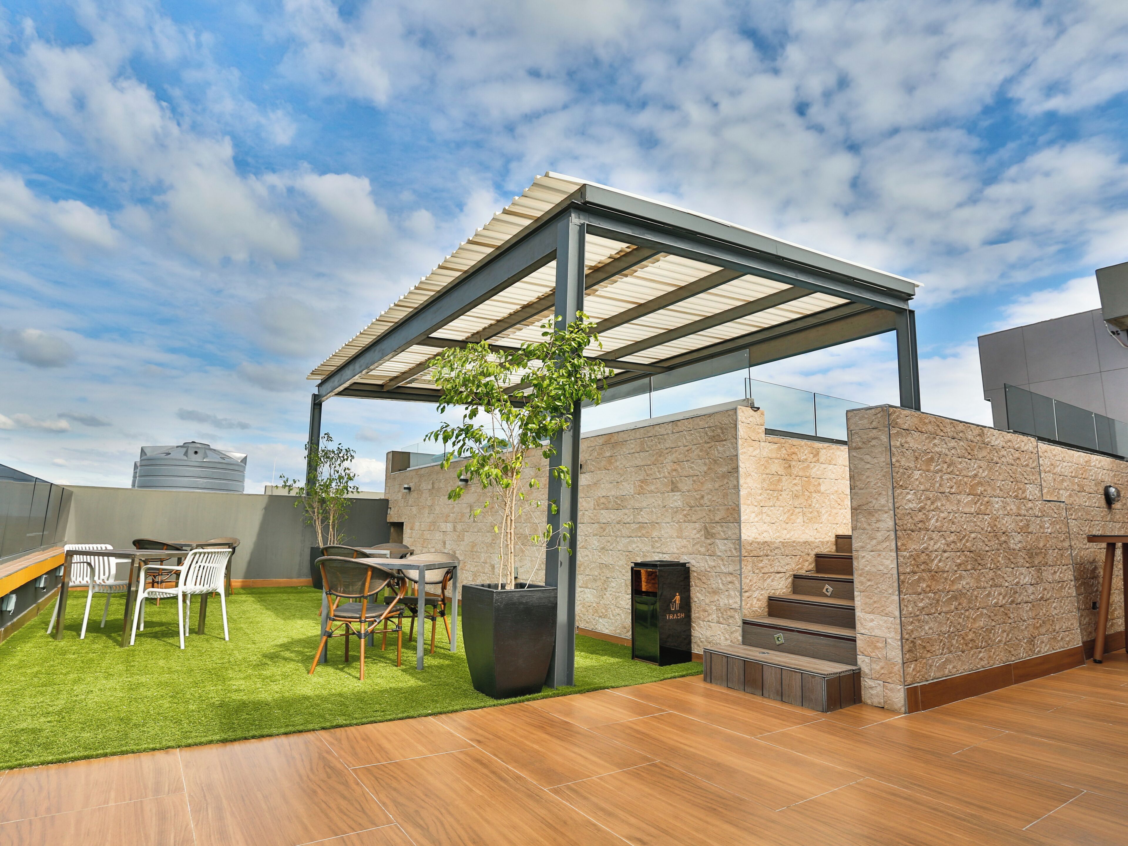 Um terraço no telhado com pérgola, mobiliário de exterior, um contentor de lixo e uma escadaria.