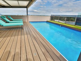 Piscina no terraço com deck de madeira e espreguiçadeiras.