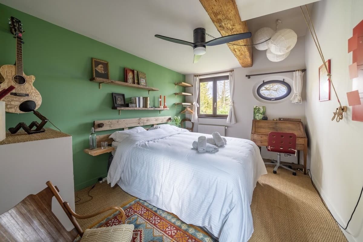 Quarto com cama, um violão, estantes de livros, uma escrivaninha e uma janela.