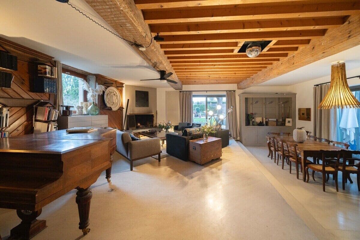 Uma sala ampla com teto de madeira, lareira, mesa de jantar com cadeiras e cozinha ao fundo.