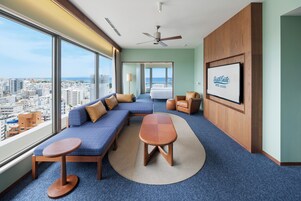 Quarto de hotel com uma janela grande, uma cama, um sofá, uma mesa e uma televisão.
