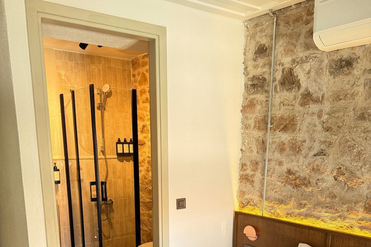 Quarto de hotel com cama, banheiro com chuveiro e parede de pedra.