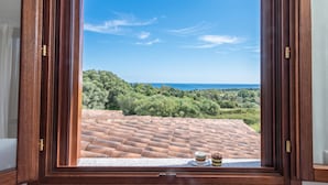 Uma janela de madeira com vista para um telhado de telhas de barro e uma xícara e pires no parapeito.