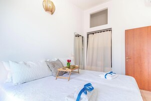 Uma cama bem arrumada com uma toalha azul, uma mesa de cabeceira de madeira com um vaso de flores e um travesseiro listrado.