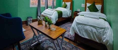 Quarto com duas camas, uma mesa pequena com uma planta, uma cadeira e uma janela com cortinas.
