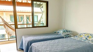 Quarto com duas camas, uma rede e vista para um prédio.
